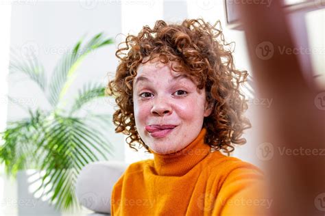 Crazy Young Female With Curly Hair Showing Tongue While Taking Selfie