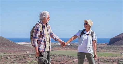 건강한 라이프스타일과 화창한 날을 즐기는 산에서 하이킹을 하는 행복한 활동적인 노부부 두 노인이 손을 잡고 웃으며 물 위에 수평선을 놓습니다 휴가와 스포츠 개념 사진