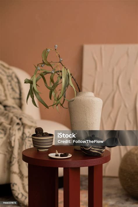 나무 둥근 커피 테이블 잎이 달린 베이지색 꽃병 컵에 담긴 차 주전자 및 개인 액세서리가 있는 거실 인테리어의 창의적인 구성