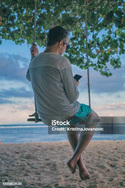 남자 나무 그네에 앉아서 열 대 해변에서 핸드폰을 사용 하 여 관광객에 대한 스톡 사진 및 기타 이미지 관광객 그네 나무 Istock