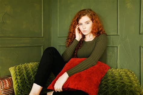 Premium Photo Curly Redhead Girl Sitting At The Sofa Around The Pillows In The Green Interior