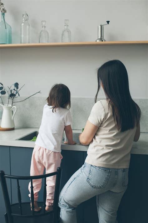 Mom And Two Year Old Daughter Wash Vegetables In The Kitchen Sink Back