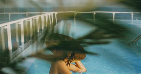 모자를 쓴 세련된 젊은 여성이 야자수 잎 아래 수영장에서 휴식을 취하고 여름 휴가에 따뜻한 햇살을 즐기고 있습니다 고급 열대 리조트에서 휴가를 보내는 햇볕을 쬐는 소녀