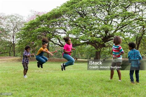 아프리카계 미국인 아이들이 공원에서 밧줄을 뛰어 넘는 재미를 가지고 있습니다 야외에서 밧줄을 뛰어 넘는 쾌활한 아이 녹색 잔디에서 함께 노는 것을 즐기는 행복한 흑인 줄넘기