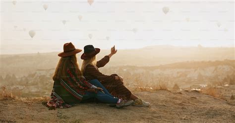 여행하다 하늘에서 열기구를 날리는 여성 여행자 언덕에 앉아 일몰을 즐기는 모자를 쓴 여성 고해상도 사진 Unsplash의 카파도키아 이미지