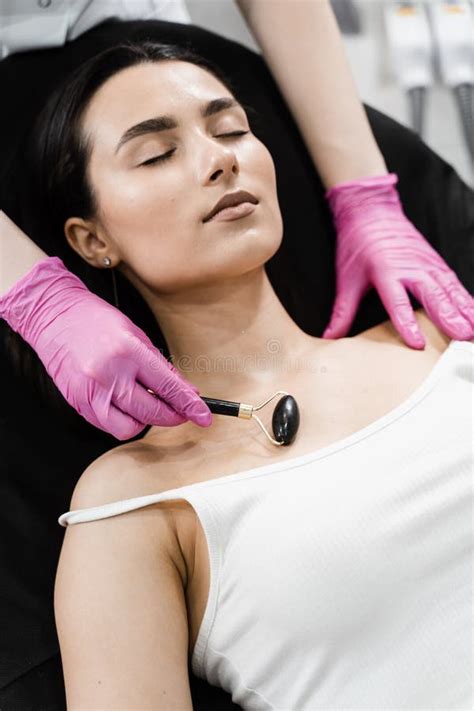 Cosmetologist Using Stone Roller For Face Massage For Girl Patient