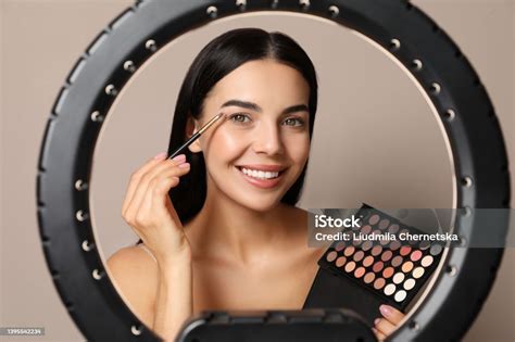 베이지 색 배경에 브러시로 아이 섀도우를 바르는 아름다운 젊은 여성 링 램프를 통해 볼 수 있습니다 25 29세에 대한 스톡 사진 및 기타 이미지 Istock