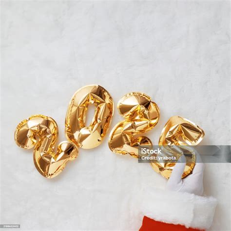 흰색 푹신한 모피 배경에 2025 년 모양의 황금 호 일 풍선을 들고 산타 손 메리 크리스마스와 새해 복 많이 받으세요 축하 개념 평면도 축제 크리스마스 겨울 휴가 카드