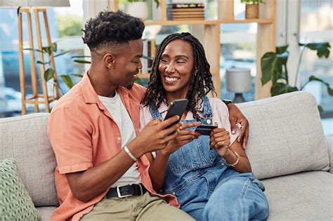 온라인 쇼핑 전화 및 신용 카드 기술이 있는 집에서 인터넷 뱅킹 앱을 위한 라운지의 소파에 있는 행복한 커플 전자 상거래 지불 및 소파에서 남자와 함께 소매 웹 사이트