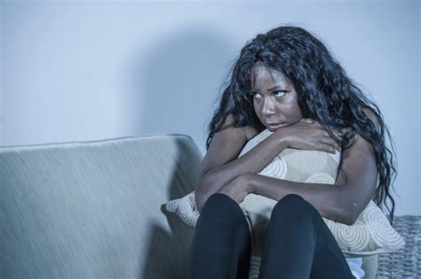 매력적이 고 슬픈 검은 흑인 여 자가 앉아 우울 가정에서 소파 소파 느낌 불안 하 고 좌절 하는 젊은 화가 보고 베개를 들고 생리 생리통 고통 30 39세에 대한 스톡 사진
