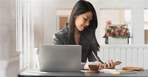 편안한 사무실을 배경으로 현대적인 작업 테이블에서 컴퓨터 노트북 앞에 앉아 메모를 하고 스마트폰을 손에 들고 보는 젊은 사업가의 사진 사진 Unsplash의 태국 이미지