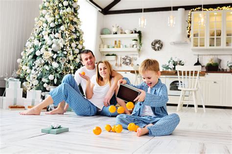 따뜻한 바닥에 앉아 파란색 잠옷을 입은 어린 소년은 부모와 크리스마스 트리의 배경에 귤이있는 선물 상자를 엽니 다 크리스마스 축하 감귤에 대한 스톡 사진 및 기타 이미지