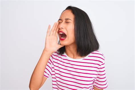 줄무늬 티셔츠를 입은 젊은 중국 여성이 고립된 흰색 배경 위에 서서 입을 다물로 큰 소리로 외치고 비명을 지르고 있습니다 통신 개념입니다 T 셔츠에 대한 스톡 사진 및 기타