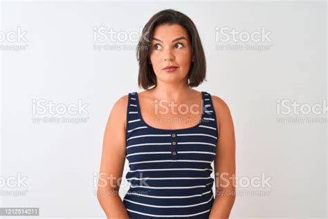 파란색 줄무늬 티셔츠를 입은 젊은 아름다운 여성이 고립된 흰색 배경 위에 서서 옆을 바라보며 생각하고 있는 미소를 짓고 있습니다 T 셔츠에 대한 스톡 사진 및 기타 이미지