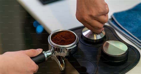 아시아 남자 커피 숍 파트 타임 직원은 커피 머신에서 뜨거운 커피를 양조합니다 커피 메이커에서 분쇄 커피로 에스프레소를 만드는