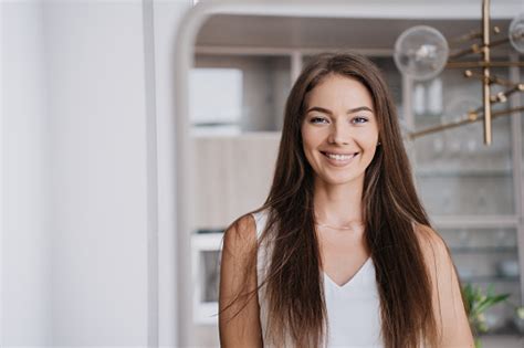 하얀 블라우스를 입은 쾌활한 젊은 백인 여성이 거울에 서서 활짝 웃으며 만족스러운 얼굴로 카메라를 바라본다 완벽한 피부를 가진 성공적인 사업가 집에서 패션 모델입니다 미용과