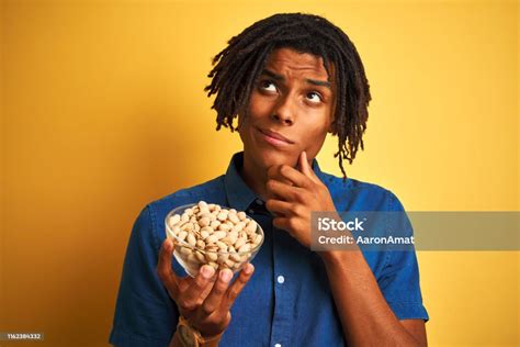 고립 된 노란색 배경 심각한 얼굴을 통해 피스타치오를 먹는 공포를 가진 젊은 아프리카 계 미국인 남자 질문에 대해 생각 매우 혼란 스러운 아이디어 개념에 대한 스톡 사진 및