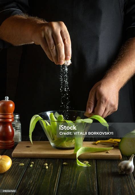 숙련된 요리사가 야채와 향신료로 둘러싸인 신선한 재료가 담긴 생생한 그릇에 소금을 뿌리고 따뜻한 조명이 켜진 주방에서 요리 준비의 예술성을 강조합니다 건강한 생활방식에 대한
