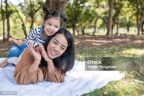 아시아 딸은 어머니를 타고 다시 복사 공간과 햇빛 아래 공공 정원에서 땅에 누워 귀여운 소녀는 매우 행복하고 재미있다 엄마와 함께 놀고 있는 보육원에서 시간을 보내고