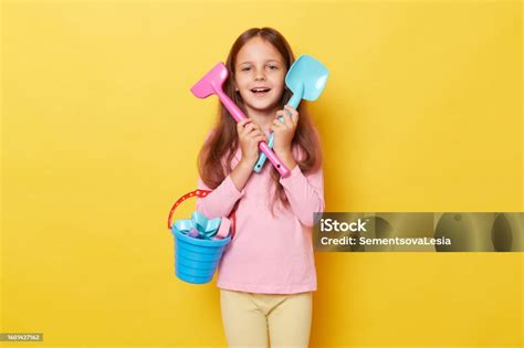 검은 머리를 가진 행복한 긍정적인 작은 귀여운 소녀가 해변 샌드박스 장난감 갈퀴와 삽을 들고 노란색 배경 위에 고립되어 여름을 즐기며 즐거운 시간을 보내고 있다 8 9 살에