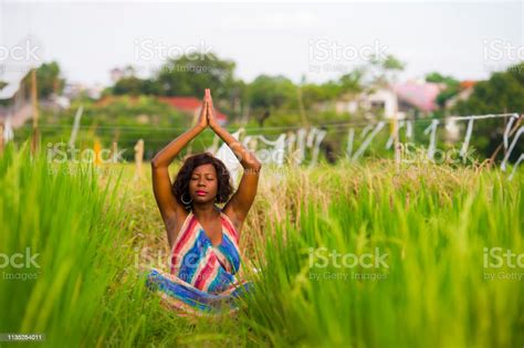 젊은 아름 답 고 행복 한 흑인 아프리카계 미국인 여자 논 야외에서 앉아 연습 요가 휴식과 명상을 즐기는 열 대 목적지에서 휴일 쾌활 한 미소 명상하기에 대한 스톡 사진 및