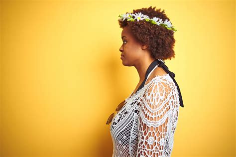 노란 고립 된 배경 위에 꽃 왕관을 입고 아프로 머리를 가진 젊은 아프리카 계 미국인 여성은 자신감있는 미소로 자연스러운 얼굴로 프로필 포즈를 취합니다 곱슬 머리에 대한