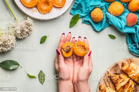 크루아상과 흩어진 살구가 있는 가벼운 주방 책상에 커널이 달린 반쪽 살구를 들고 있는 여성 손 과일에 대한 스톡 사진 및 기타 이미지 Istock