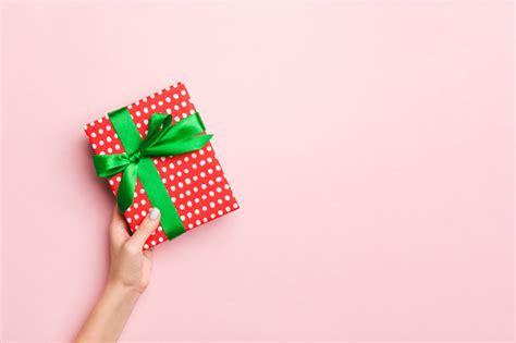 살아있는 산호 배경에 컬러 리본 줄무늬 선물 상자를 들고 여성의 손 크리스마스 컨셉 이나 다른 휴일 핸드메이드 선물 상자 카피 스페이스와 컨셉 탑 보기 Diy에 대한 스톡