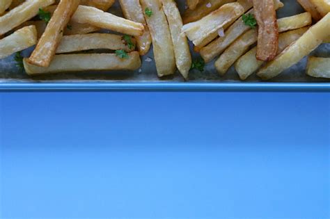 갓 요리한 바삭한 수제 감자튀김 기름칠 양피지가 늘어선 베이킹 트레이 다진 파슬리와 소금으로 장식된 황금빛 갈색 칩 더미 파란색 배경 높은 보기 복사 공간의 클로즈업 이미지