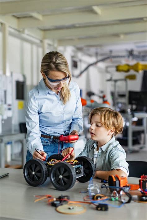 Female Teacher Helping Young Schoolboy To Build Robotic Car In After