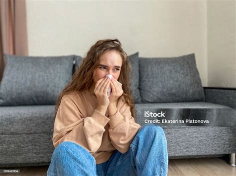 슬프고 화가 난 젊은 여성이 거실에 앉아 있는 물과 알약 한 잔을 들고 아프다고 느낍니다 감기와 독감에 대한 스톡 사진 및 기타 이미지 감기와 독감 건강관리와 의술