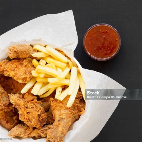 맛 있는 패스트 푸드 프라이드 치킨 드럼 스틱 매운 날개 감자 튀김 및 종이 상자에 치킨 스트립 검은 배경에 새 콤 달콤한 소스 평면도 평평한 평 신도 오버 헤드 위에서