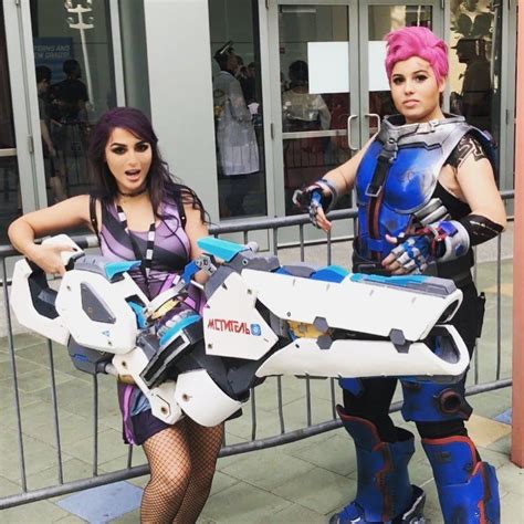 Two Women Dressed In Cosplay Costumes Standing Next To Each Other Near A Fence
