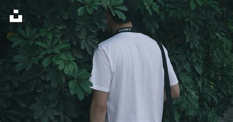 흰 티셔츠와 검은 바지를 입은 남자가 녹색 잎 근처에 서 있다 사진 Unsplash의 무료 사람 이미지