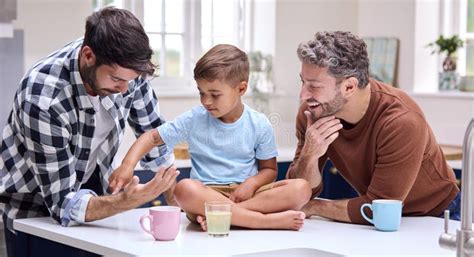 Same Sex Family With Two Dads In Kitchen With Son Sitting On Counter Stock Photo Image Of