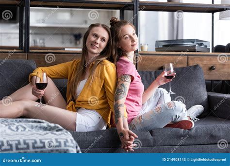 Two Smiling Lesbians Holding Wine Glasses And Holding Hands While