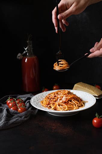 토마토 소스와 파마산을 곁들인 파스타 어두운 배경에 파스타와 흰색 접시 포크와 스파게티와 숟가락을 들고 여성의 손 포크에