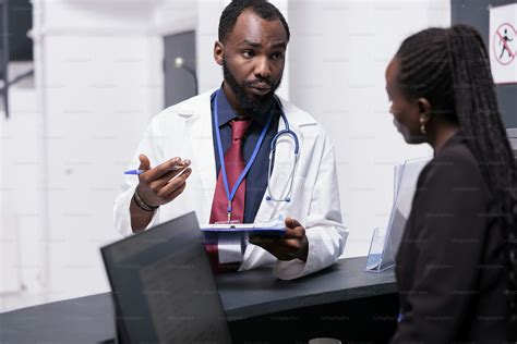 리셉션 카운터에서 의료 보험 지원 및 약속에 대해 접수원과 이야기하는 일반 개업의 의사는 진료소 로비에서 의료진과 검진 방문에 대해 논의합니다 사진 Unsplash의