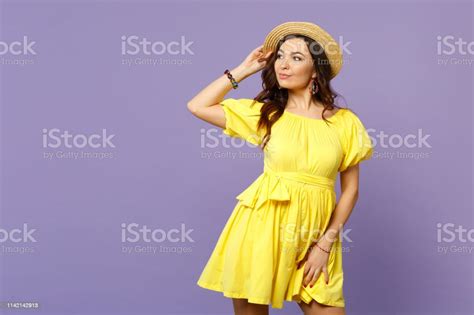 여름 모자에 손을 유지 노란색 드레스에 예쁜 젊은 여자의 초상화 스튜디오에서 파스텔 바이올렛 배경에 고립 된 찾고 사람들은 진심으로 감정 라이프 스타일 개념입니다 복사