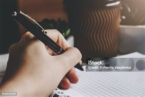 여성의 손은 펜을 들고 어두운 배경의 노트북에 씁니다 왼손잡이 소녀는 노트북 어두운 토닝 사진에 메모를 남깁니다 갈색에 대한