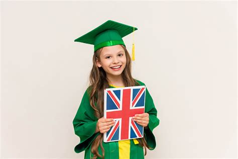 석사 복을 입은 학생이 영어로 영국 국기가 적힌 책을 들고 행복하게 웃고 있습니다 어린이를 위한 언어 교육 학교 영어 학교 졸업 흰색 격리 된 배경 8 9 살에 대한 스톡