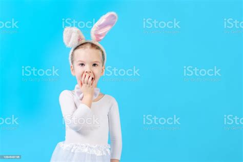 파란색 배경에 흰색 토끼 의상 어린이 토끼의 귀를 가진 귀여운 어린 소녀 그녀의 입에서 놀라운 다룹니다 텍스트를 위한 공간으로 광고 사진입니다 공휴일에 대한 스톡 사진 및