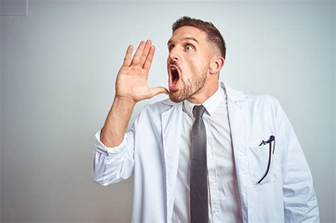 고립 된 배경에 흰색 교수형 코트를 입고 젊은 잘 생긴 의사 남자는 입에 손으로 옆으로 큰 소리로 외치고 비명을 지르고 있습니다 통신 개념입니다 과학자에 대한 스톡 사진 및