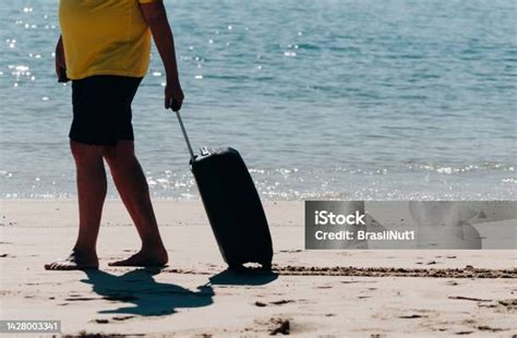청록색 바다 배경이있는 모래 사장에 검은 여행 가방을 들고 반바지와 티셔츠를 입은 맨발의 남자 여름 휴가 개념 T 셔츠에 대한 스톡 사진 및 기타 이미지 Istock