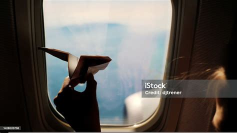 클로즈업 비행기 창문의 배경에 작은 종이 비행기가있는 어린이 손의 실루엣 항공기 창문에 앉아서 작은 종이 비행기로 노는 아이 비행기에서 비행 중 비행기에 대한 스톡 사진 및