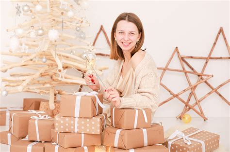 젊은 아름다운 고급스러운 금발 여자는 샴페인 한 잔을 들고 새해를 축하합니다 크리스마스 트리 많은 선물 상자와 장식의 배경으로