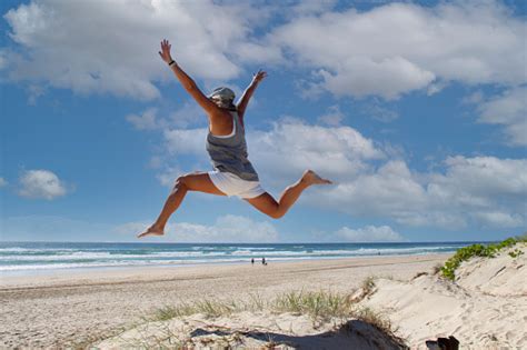 해변에서 공중에 뛰어 오르는 무두질 한 여성 백그라운드에서 모래와 바다 흰색 반바지와 회색 싱글 골드코스트 퀸즐랜드