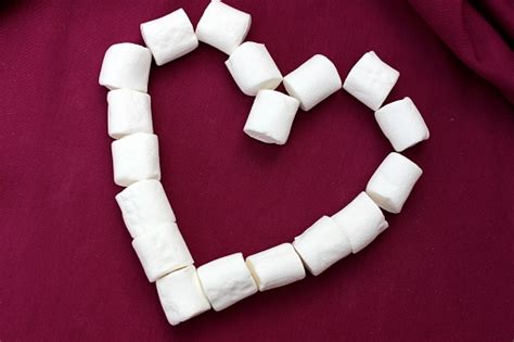 마시멜로는 분홍색 배경에 고립 된 심장모양으로 배치되었습니다 자홍색 보라색 테이블에 마음의 형태로 배치 작은 흰색 마시멜로의 무리 클로즈업에 과자 0명에 대한 스톡 사진 및