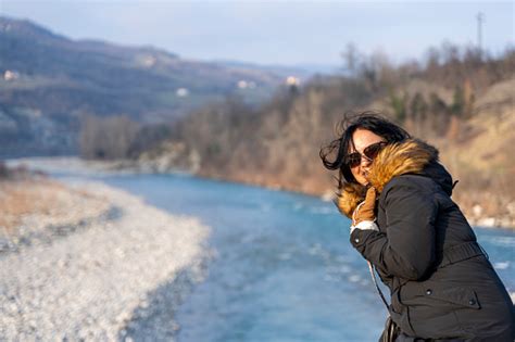 겨울 옷과 선글라스를 끼고 강과 언덕이 있는 풍경 앞에서 아름다운 중년 여성의 초상화 Brand Name Smart Phone에