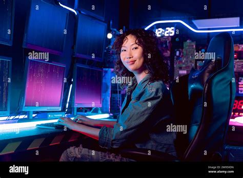 Female Asian Hacker Smiling In Hideout Place With Dark Environment And Multiple Displays And